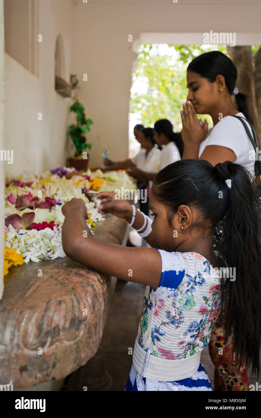 Vertical portrait of a young girl putting flowers at the altar in Jaya ...