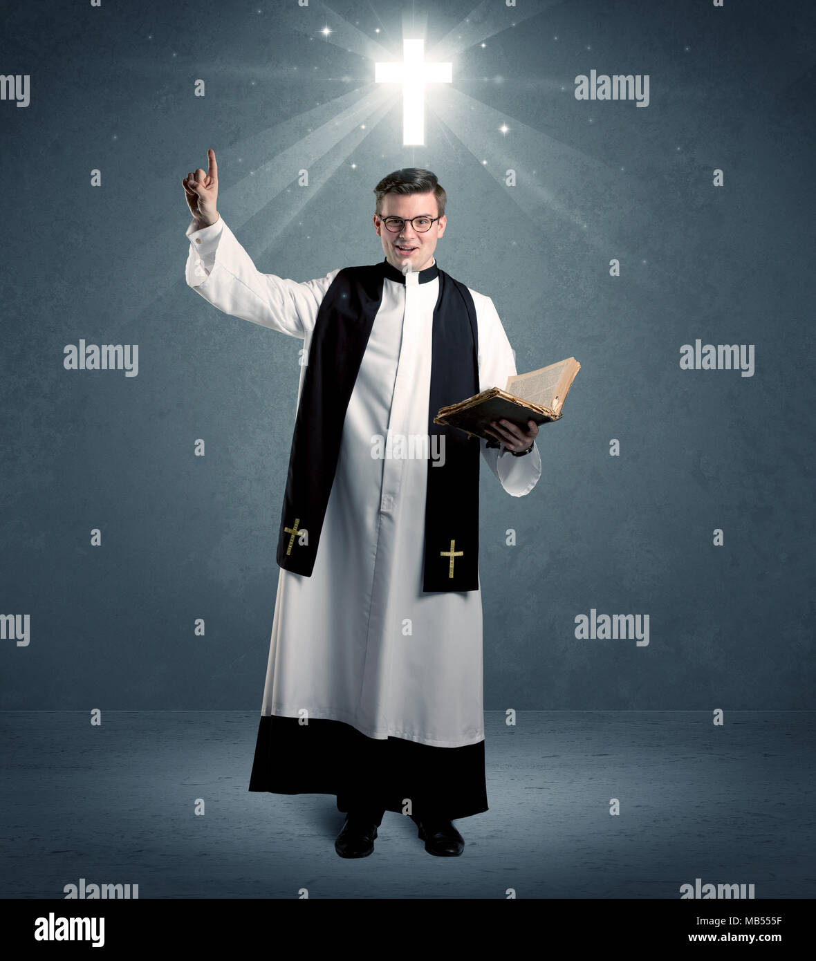 A young caucasian priest with deep faith blessing with the holy bible ...