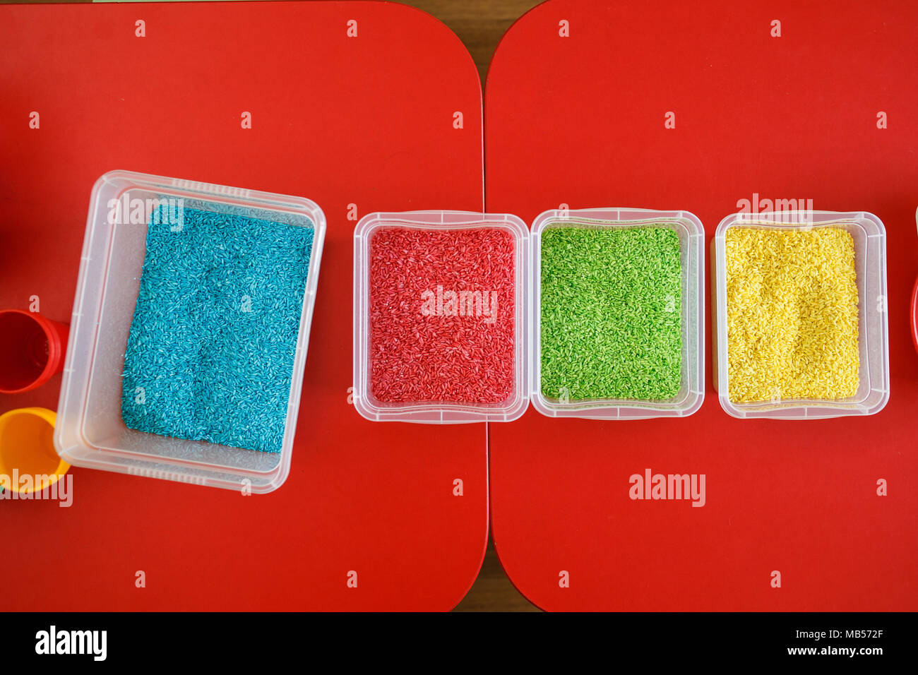 Sensory box for toddlers with colourful rice on red table. Top view ...
