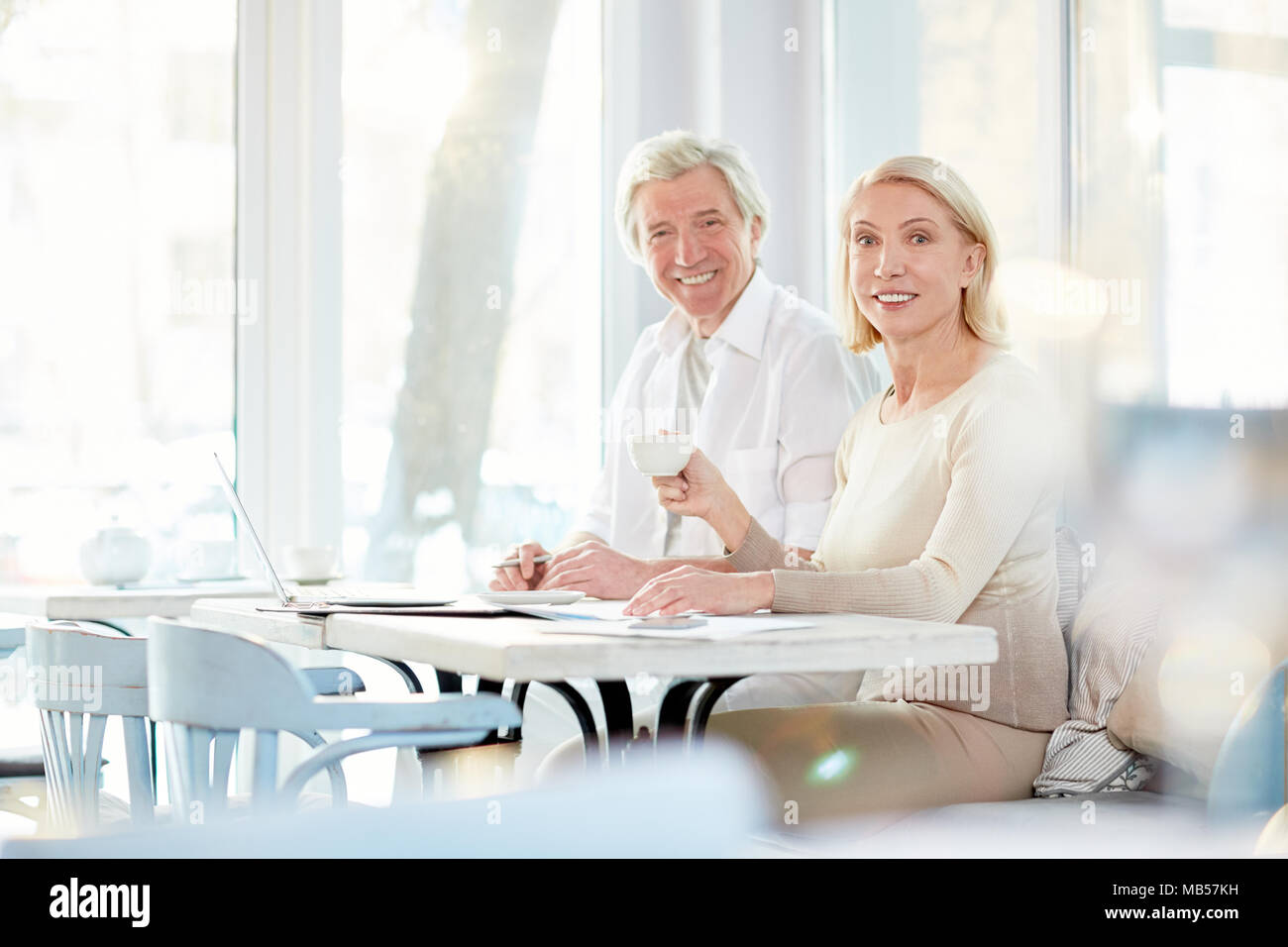 Happy mature colleagues having tea or coffee while sitting by table in ...