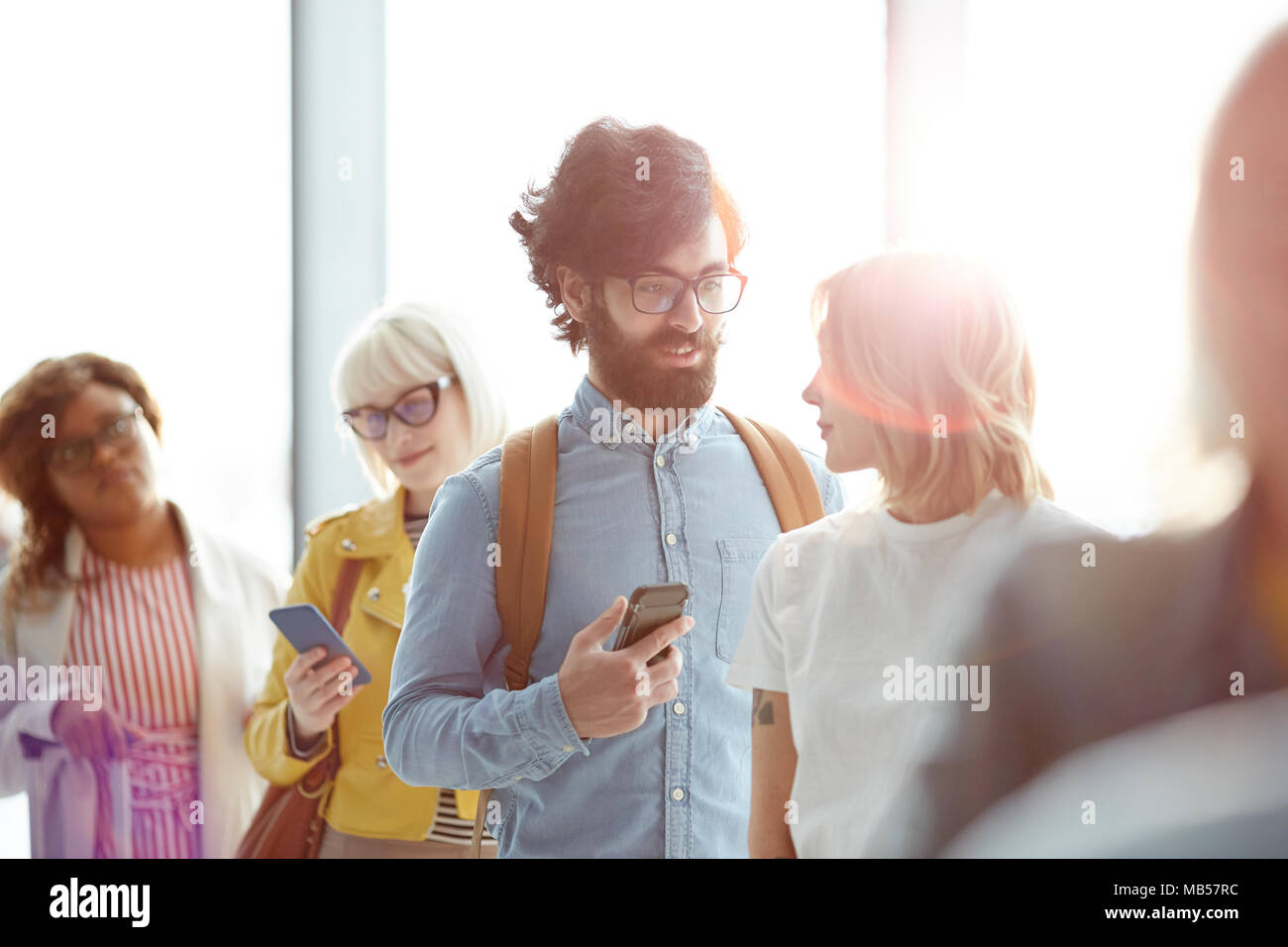 Young traveler with smartphone talking to woman in queue to check-in ...