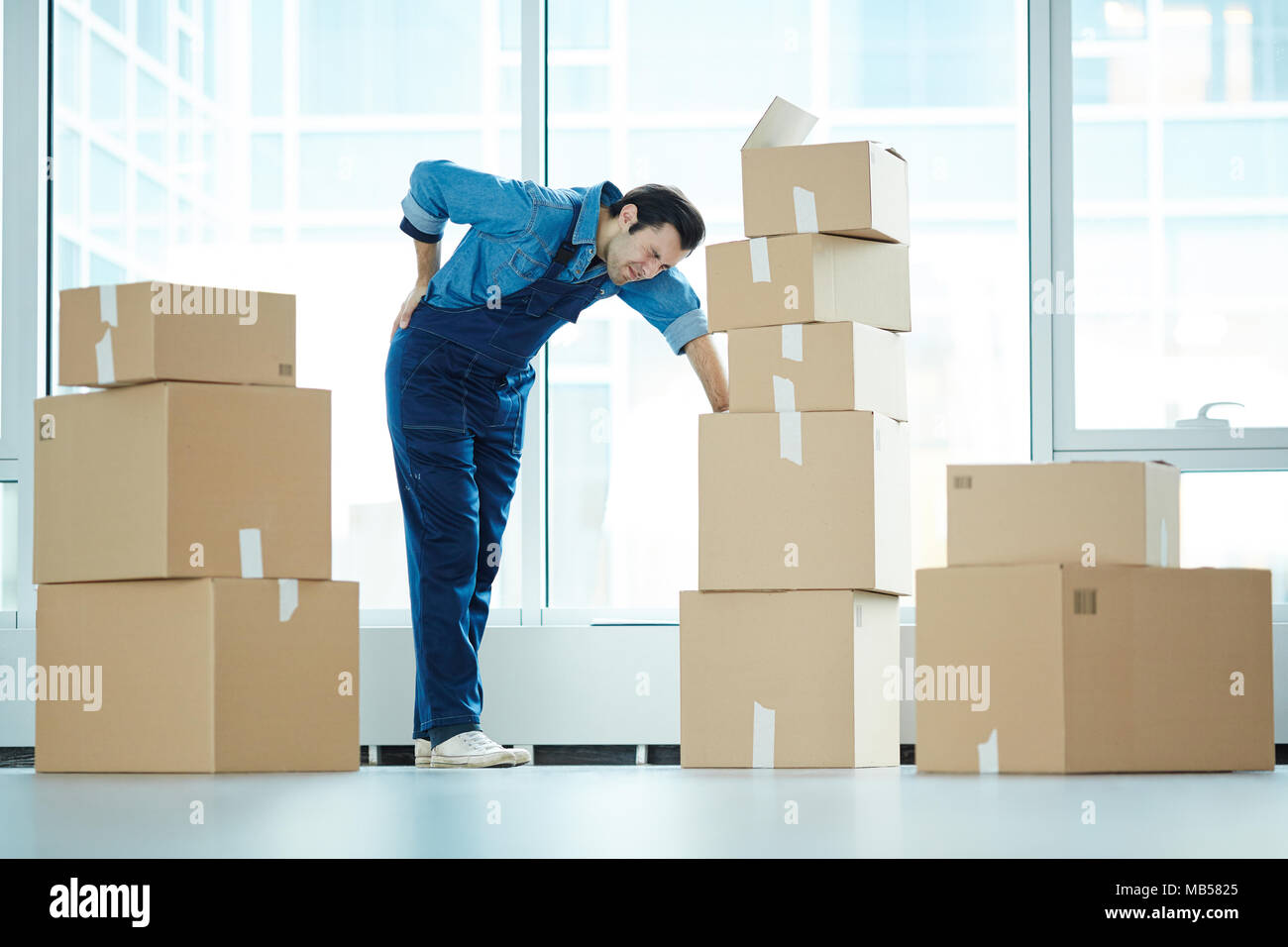 Young relocation service staff touching his back and leaning by stack ...