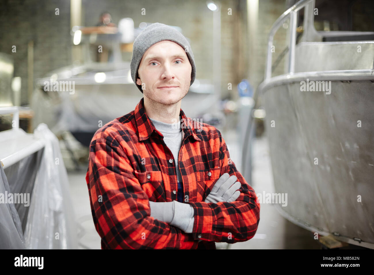 Young engineer of ship and boat industry looking at camera in hangar or ...