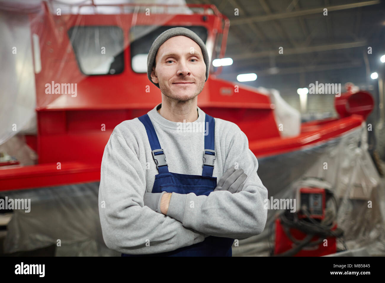 Young cross-armed engineer in workwear on background of new model of ...