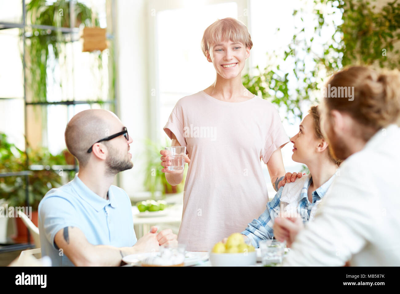 Happy girl with glass of water looking at her friends by served table ...
