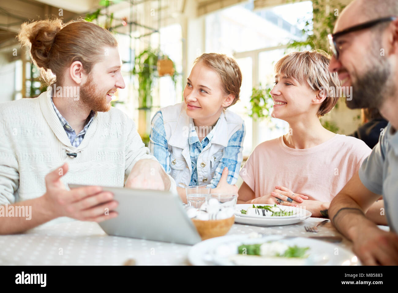 Happy girls looking at their friend with tablet while discussing ...