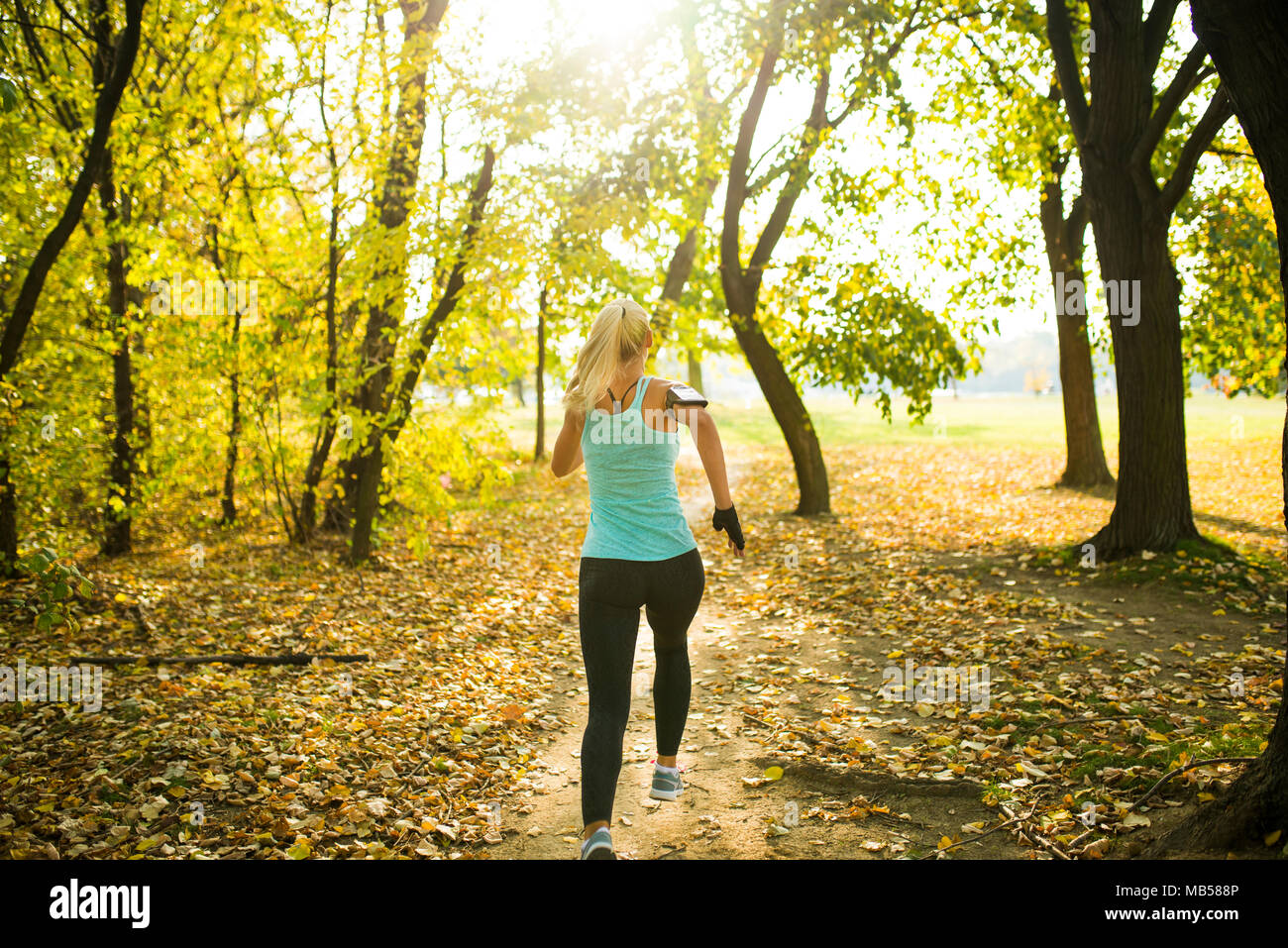 Attractive young sporty woman jogging in the park covered with leaves ...