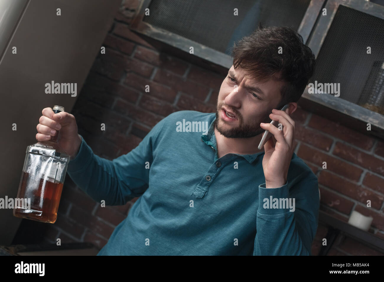 Young man alcohol addiction problems sitting at table answering phone ...