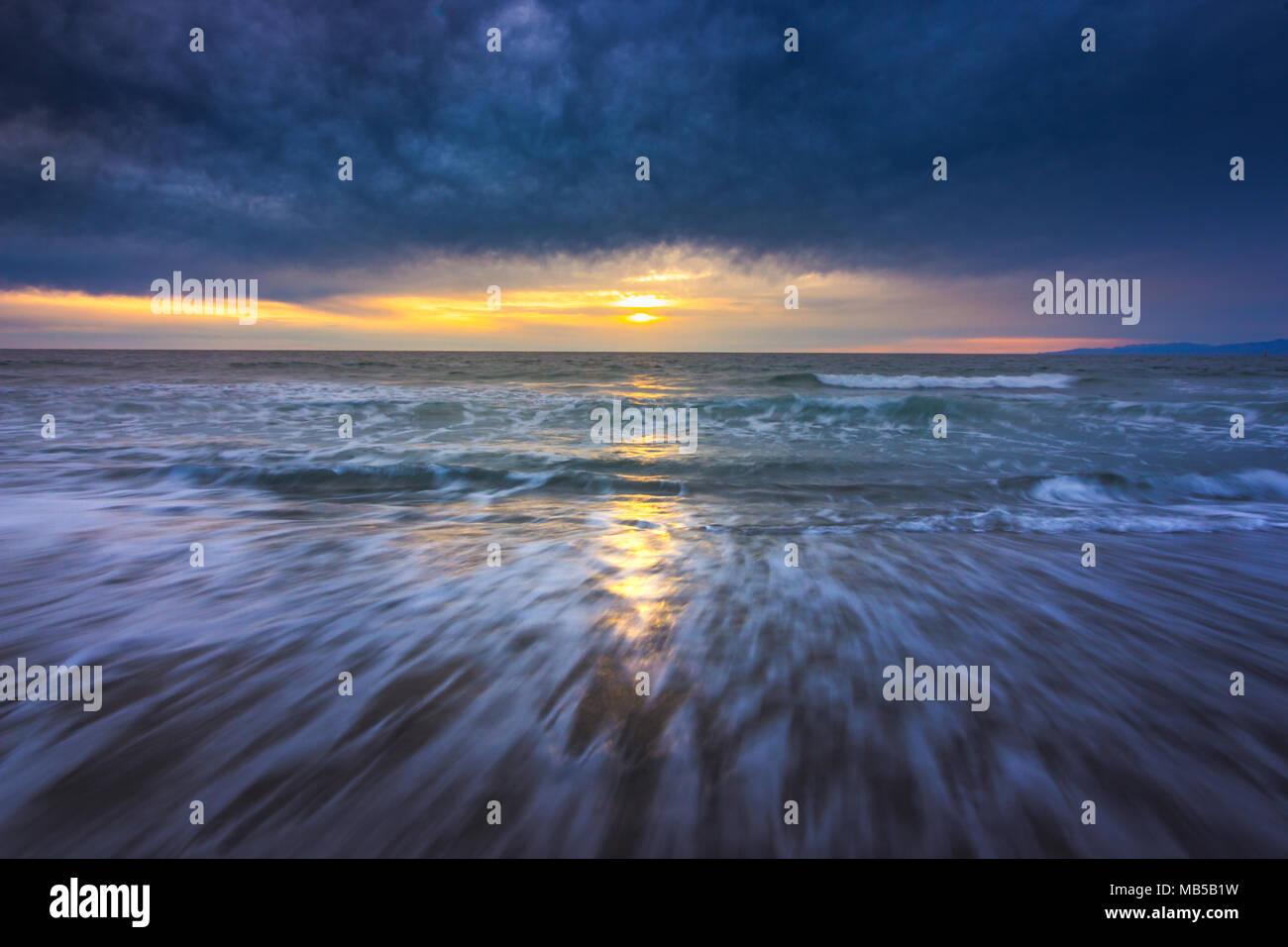 Long-exposure photograph of silky smooth waves washing onto the sandy ...