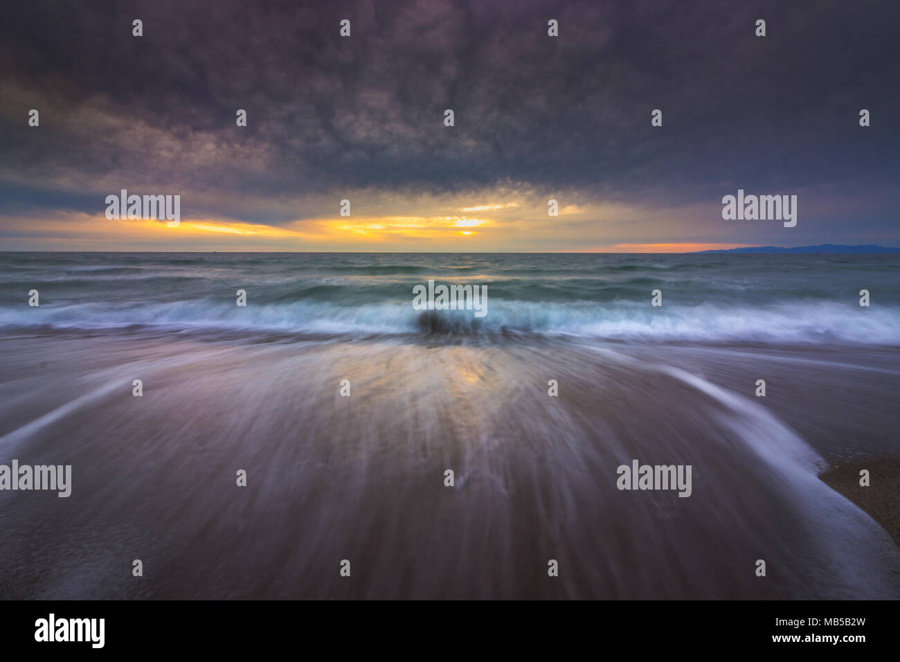 Long-exposure photograph of silky smooth waves washing onto the sandy ...