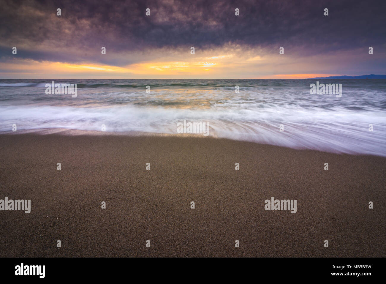 Long-exposure photograph of silky smooth waves washing onto the sandy ...