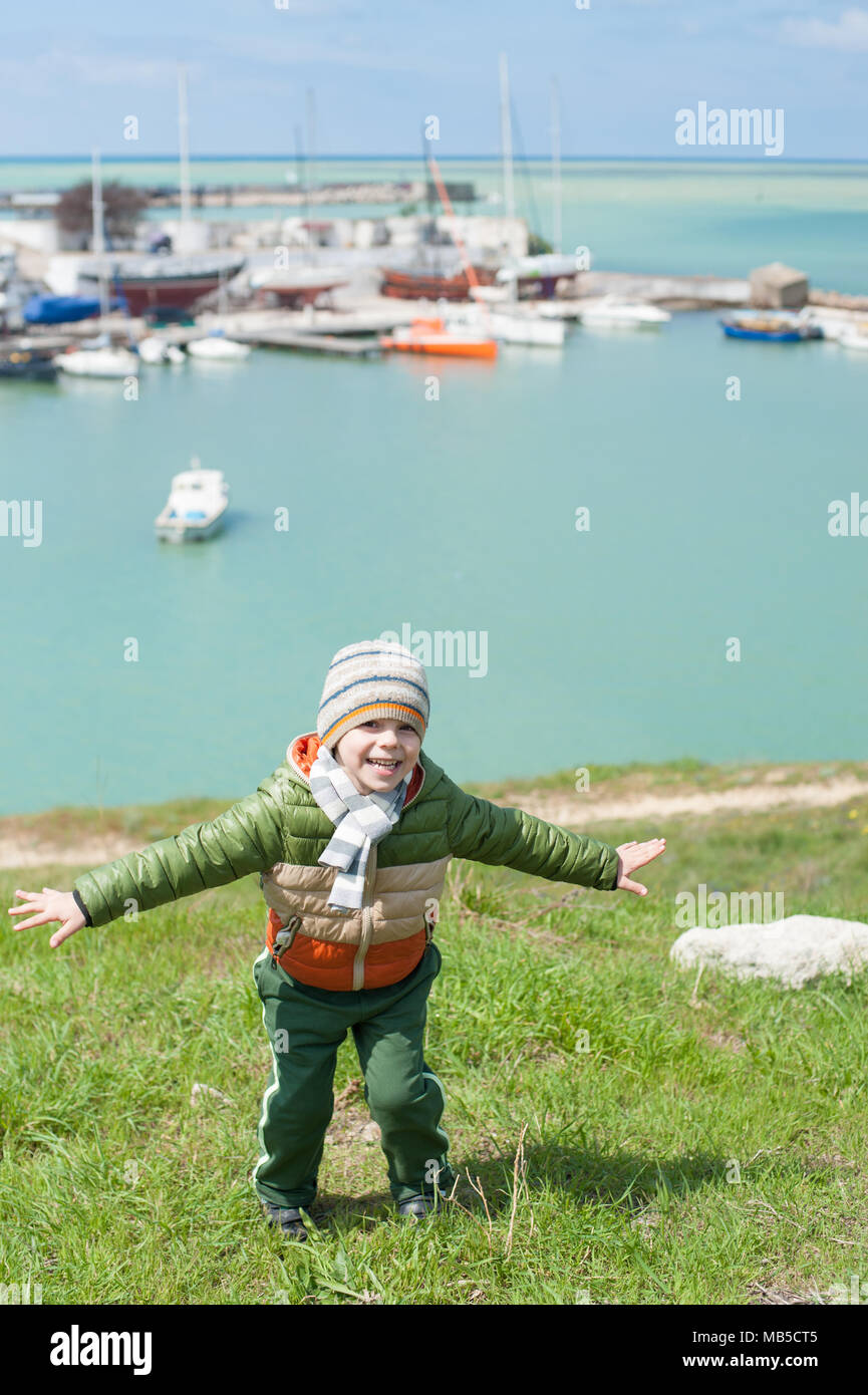 cute small boy dressed in warm jacket scarf and hat on green slope ...