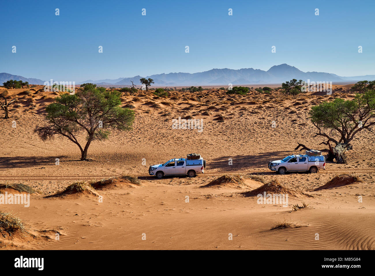 two 4x4 cars of selfdriving tourists driving through dunes of deserted ...