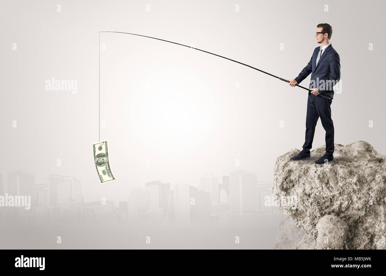 Elegant young businessman fishing cash from a huge rock Stock Photo - Alamy