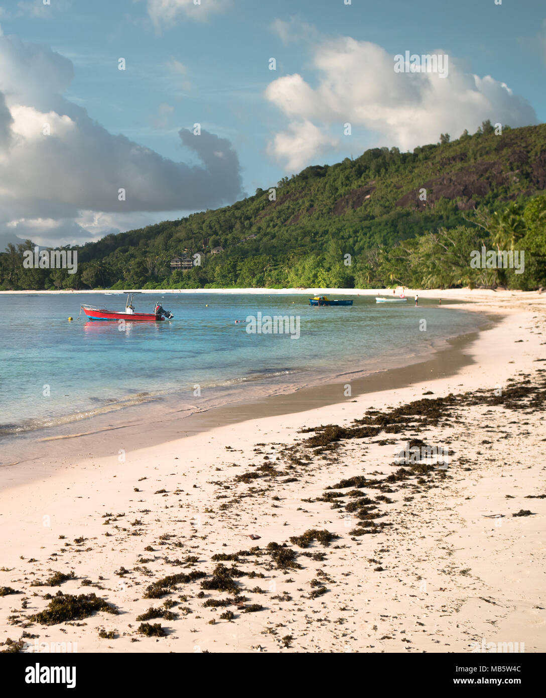 Red motor boat anchored off a sunny Seychelles beach with distant ...