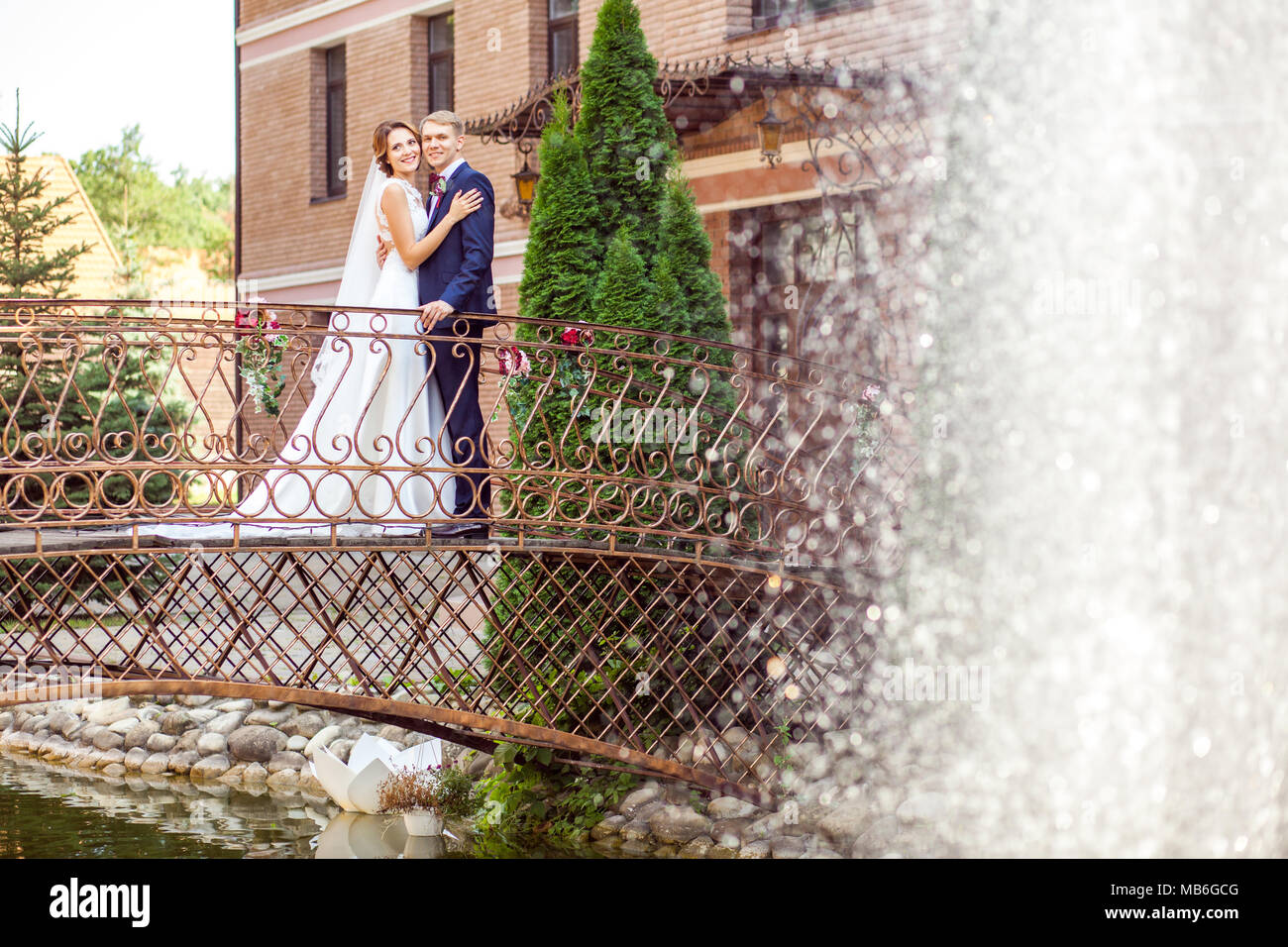 handsome groom and attractive bride hugging while standing on bridge ...
