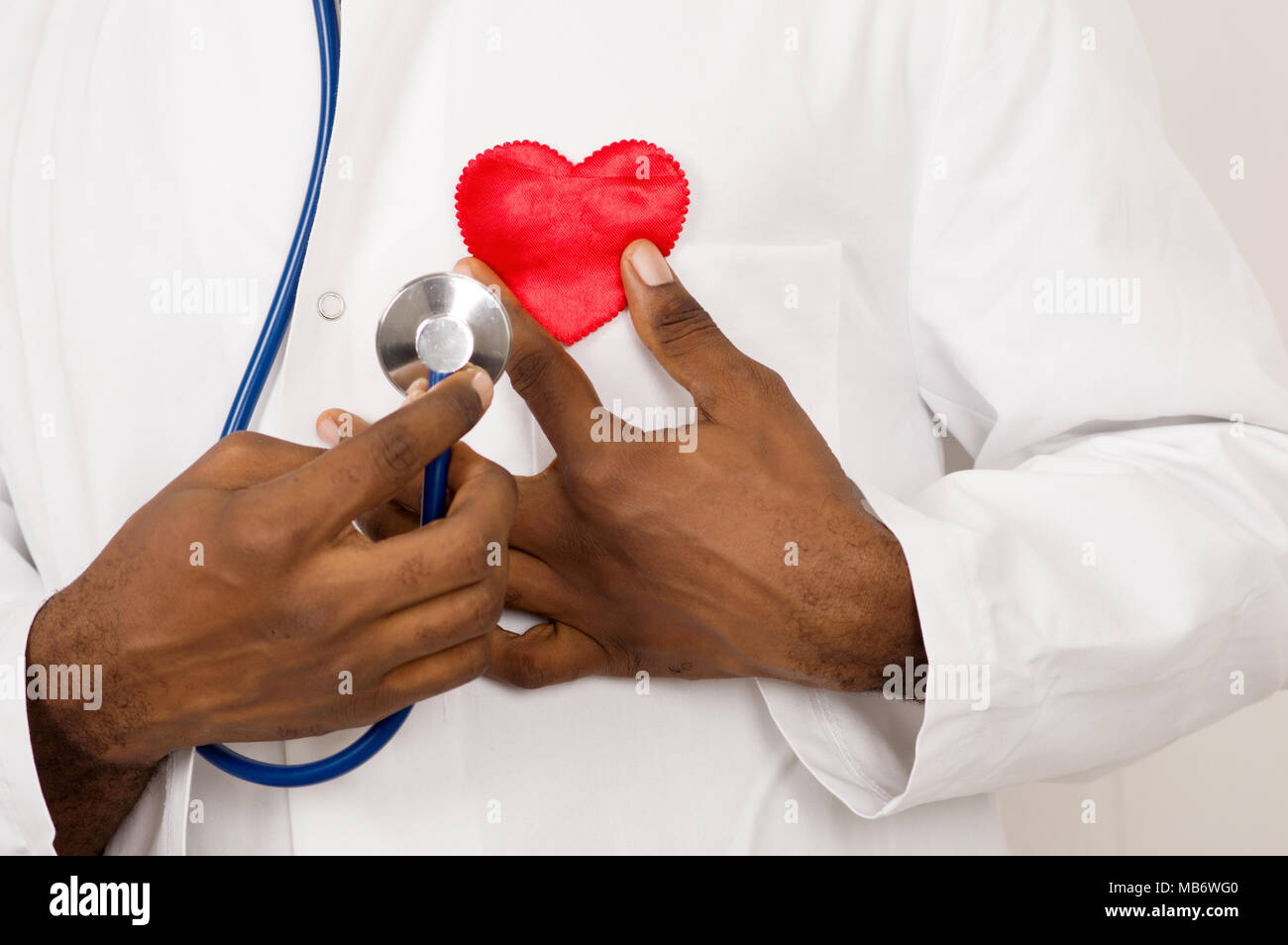 Close-up of male doctor's hands holding a red heart lying on his chest ...