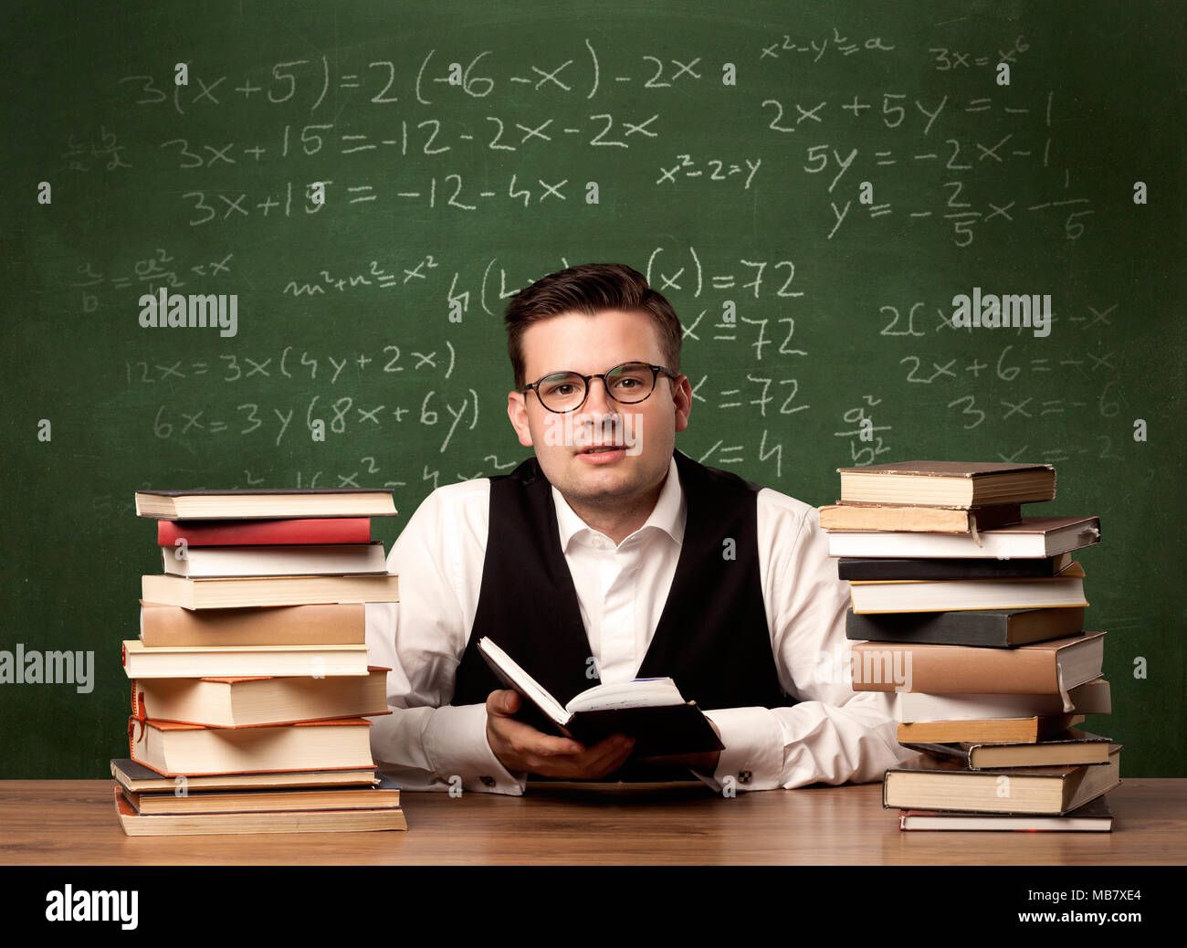 A young ambitious teacher in glasses sitting at classroom desk with ...