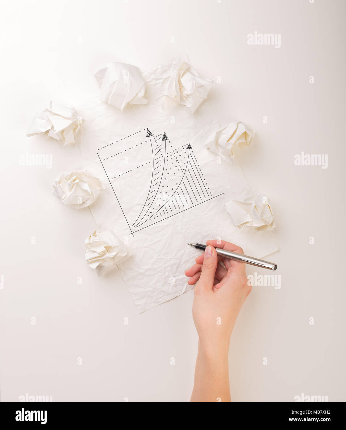 Female hand next to a few crumpled paper balls drawing a progress chart ...