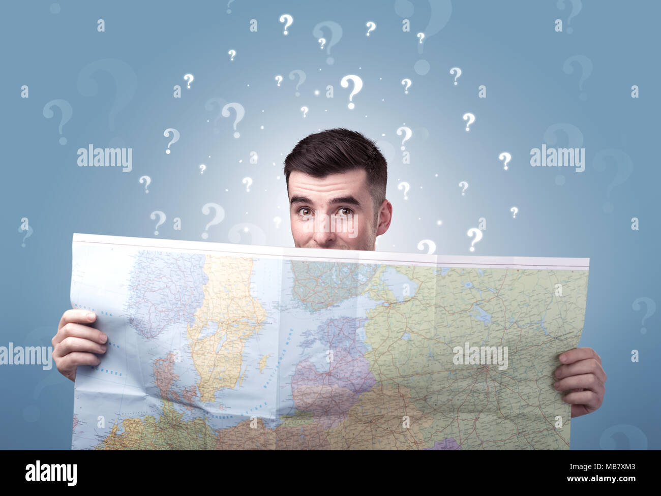 Handsome young man holding a map with white question marks above his ...