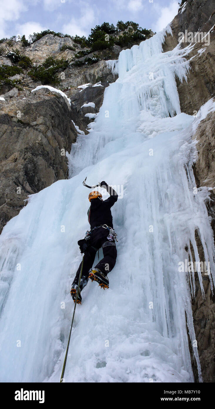 male ice climber on a steep frozen waterfall on a beautiful winter day ...