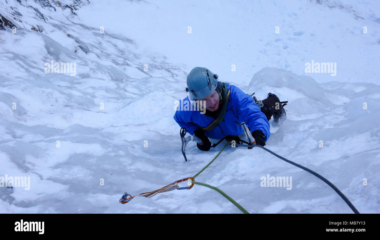 male ice climber in a blue jacket on a steep frozen waterfall in deep ...