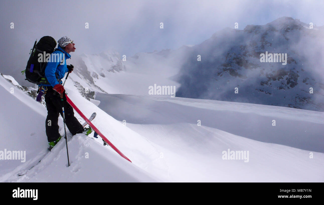 male backcountry skier on his way up to a high alpine peak and playing ...