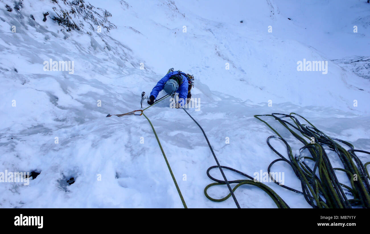 male ice climber in a blue jacket on a steep frozen waterfall in deep ...