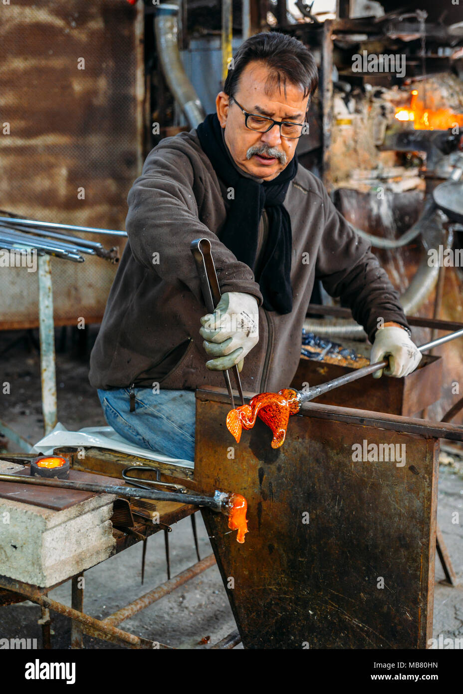 Traditional glass blower forming a beautiful piece of glass in a ...