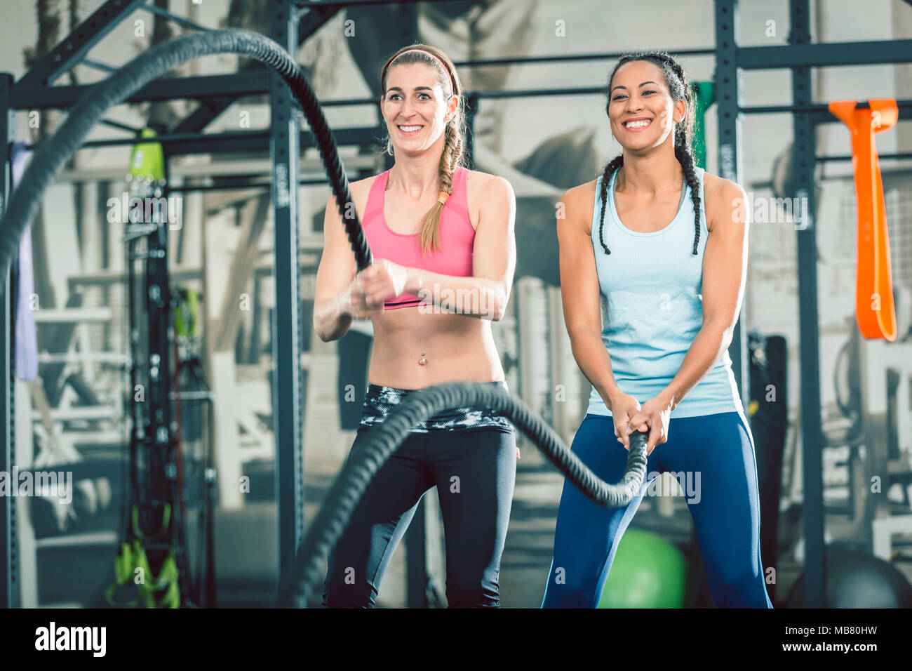 Two beautiful and strong women waving battle ropes during functional ...