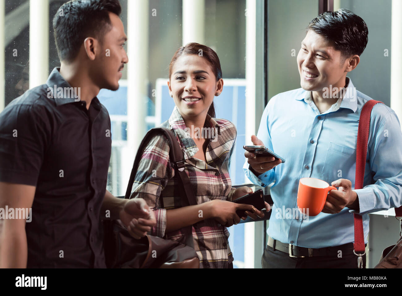 Three young and cheerful employees at their workplace talking in the ...