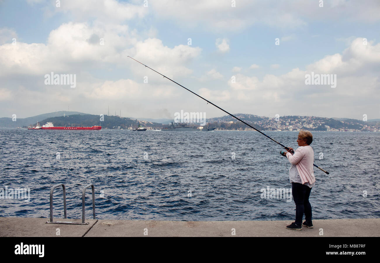 Woman try to catch fish. Dry cargo vessel and war ship cross Bosphorus ...