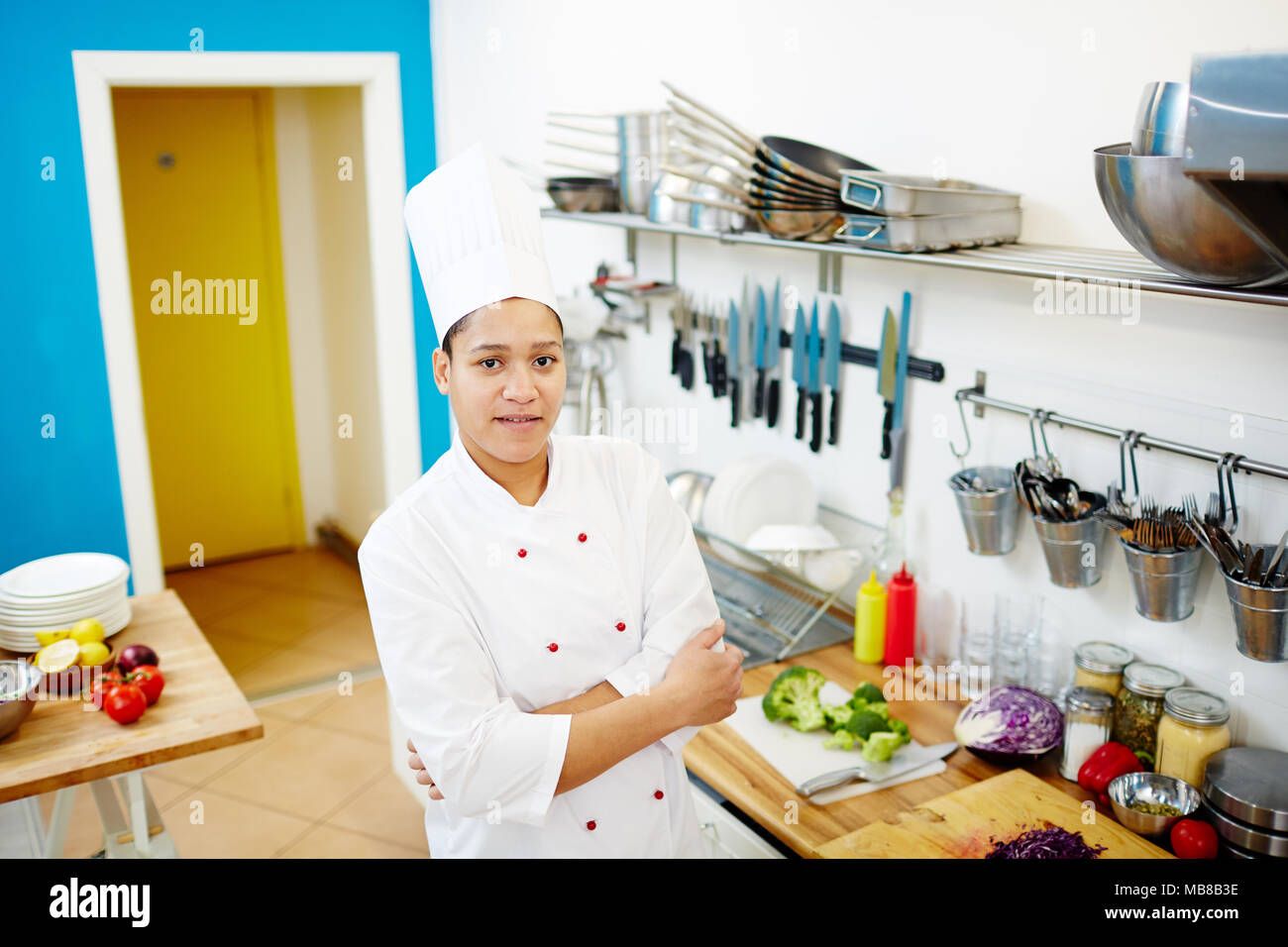 Young professional cross-armed chef looking at camera by her workplace ...