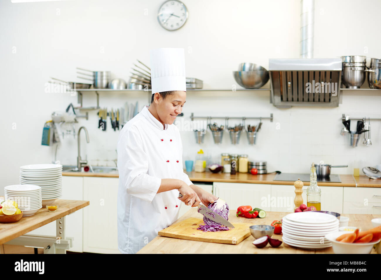 Professional chef standing by table and chopping fresh purple cabbage ...