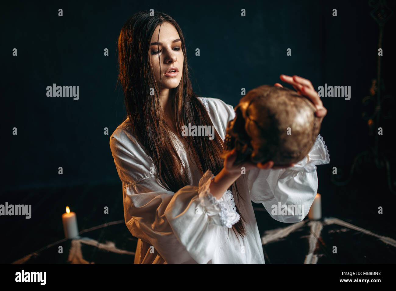 Young woman in white shirt holds human skull in hand, pentagram circle ...