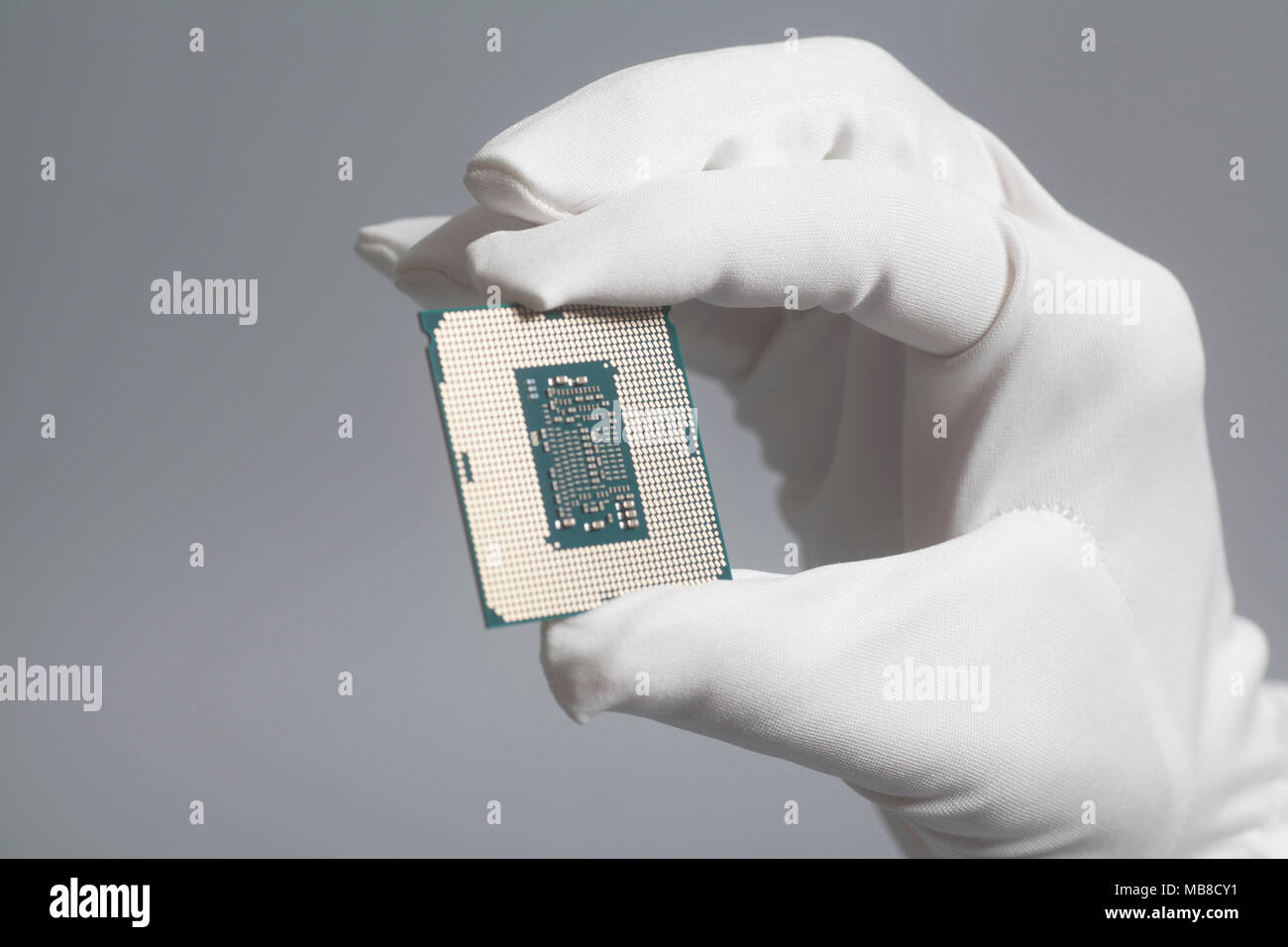Hand in white glove holding a CPU computer processor microchip on gray ...