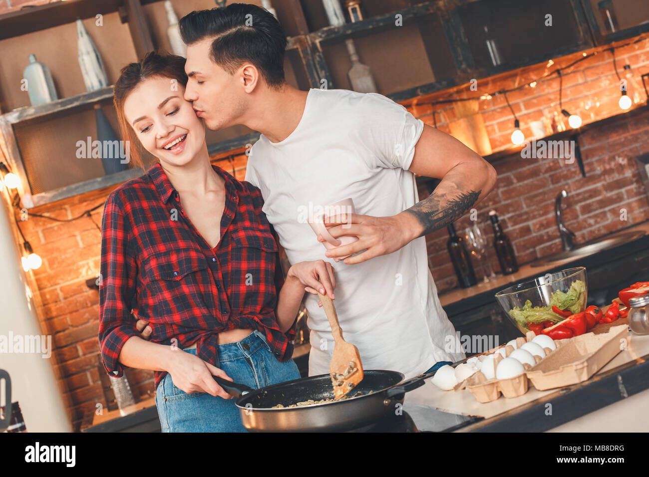 Attractive couple. Man kissing wife, she cooking dinner. Indoor ...