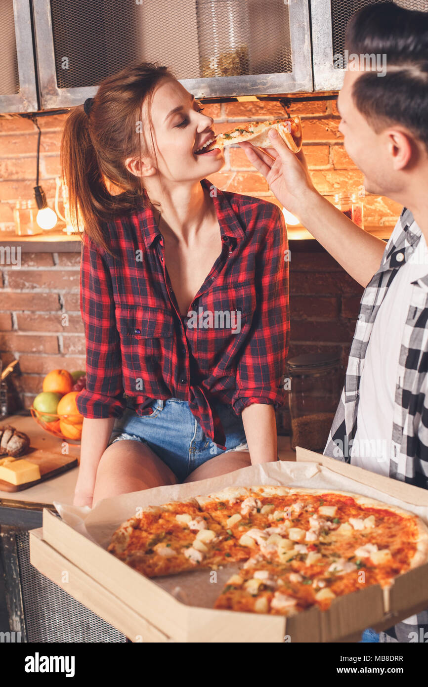 Closeup photo. Smiling man give one piece of pizza his wife. Indoor ...