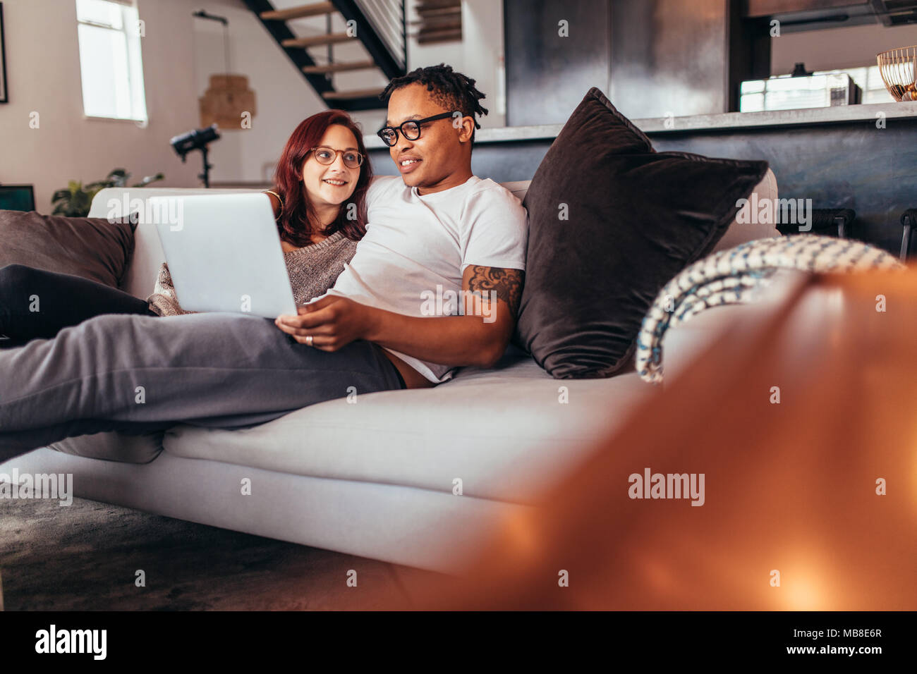 Mixed race couple sitting on a couch with laptop in living room. Couple ...