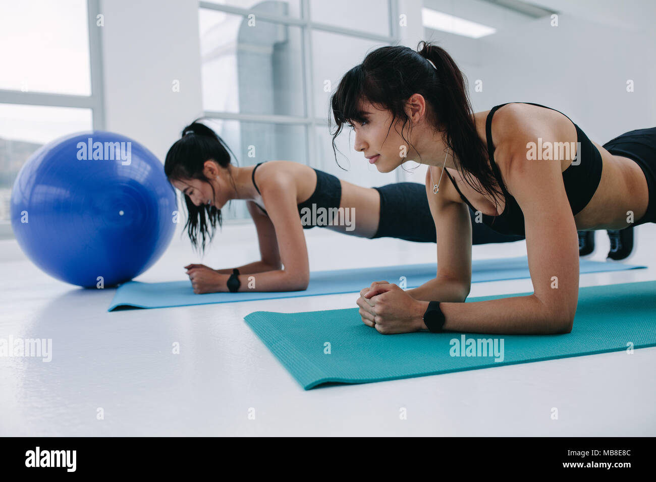 Two girls making effort while doing planks during workout in gym ...