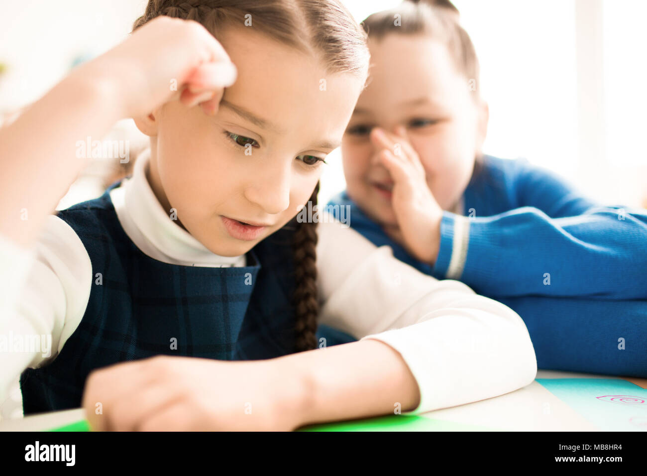 Little girl tells the answer to her neighbor at the table at lesson ...
