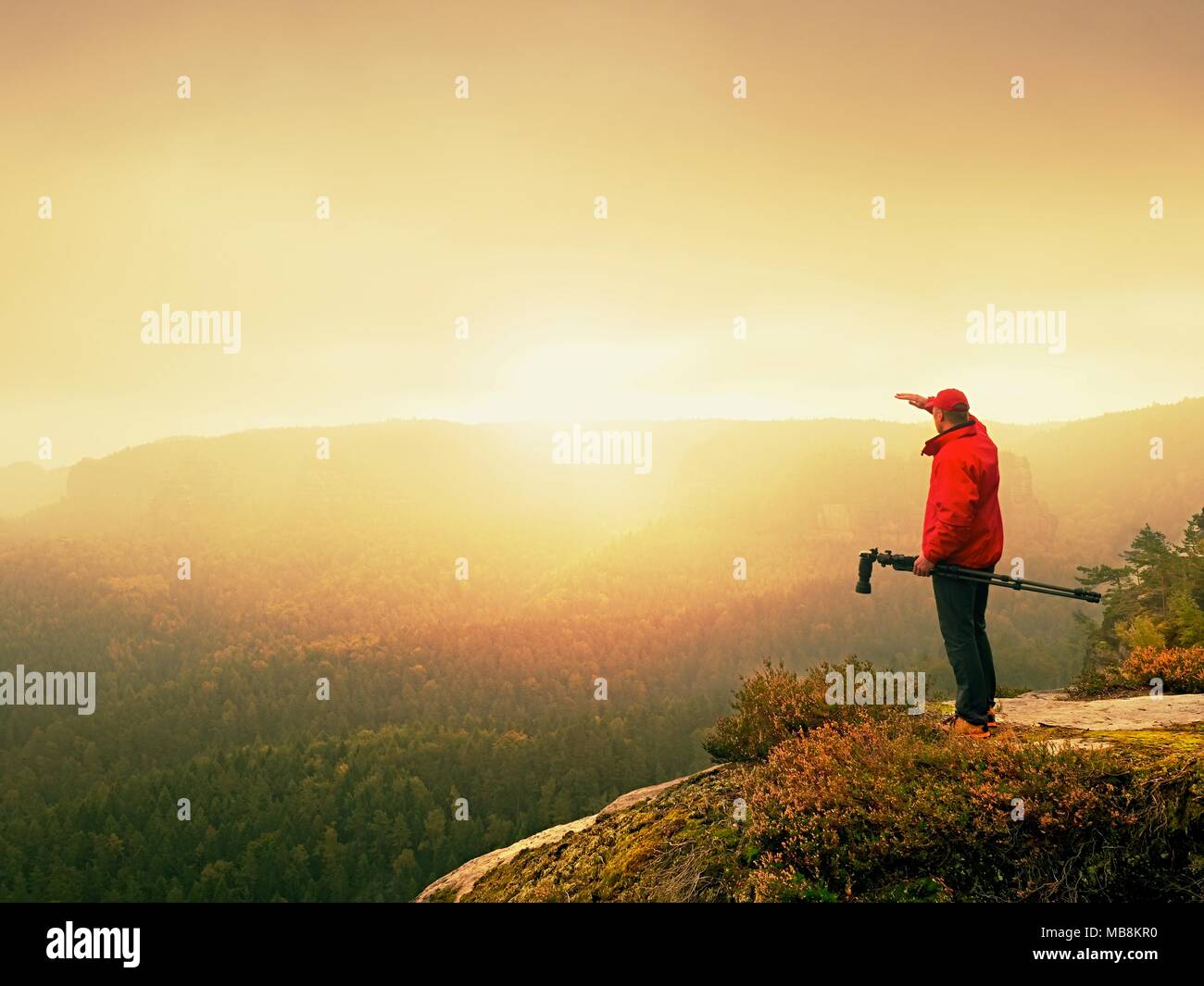 Photographer working with mirror camera and tripod on peak of rock ...