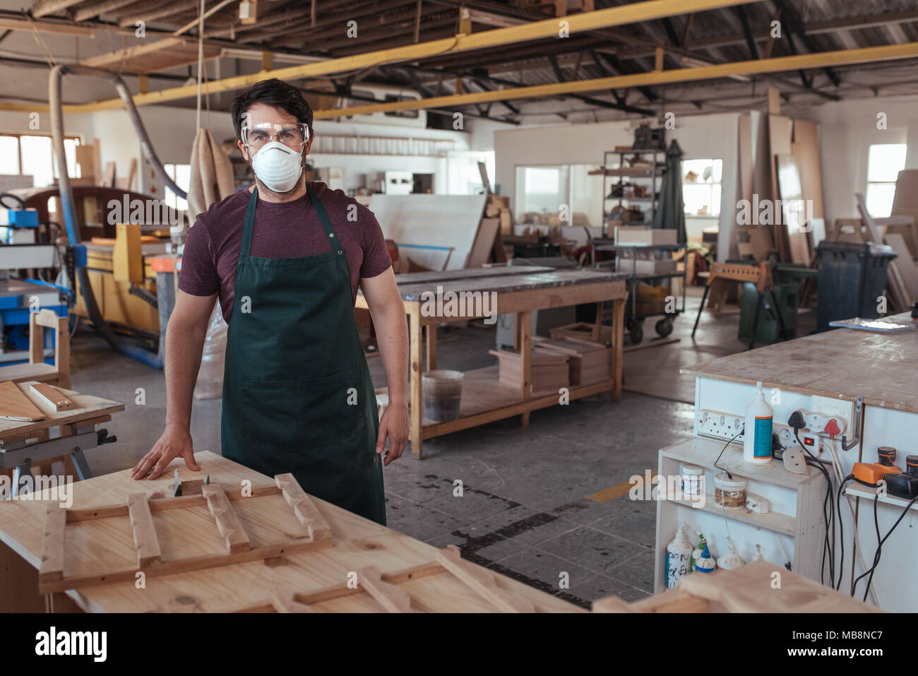 Young woodworker standing in his studio wearing protective workwear ...