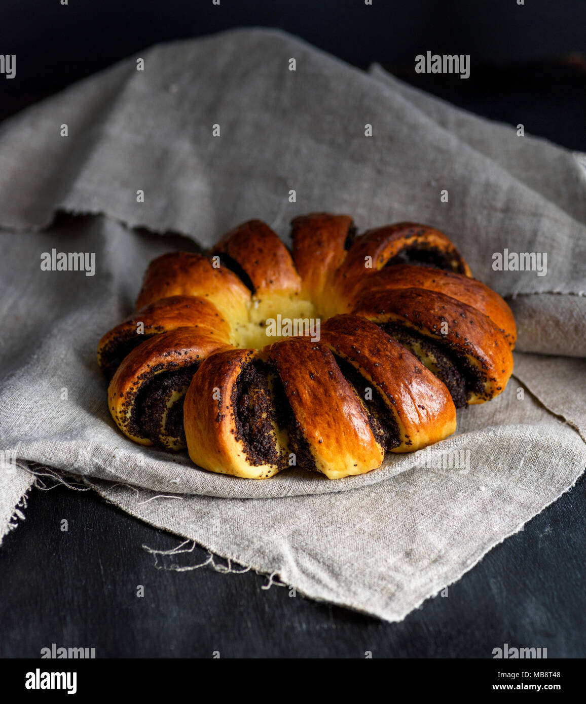 baked round pie with poppy seeds on a gray linen napkin, black wooden ...