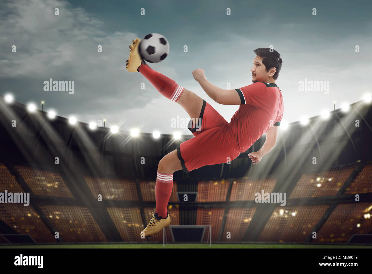 Powerful asian footballer kick the ball in the air on stadium field ...