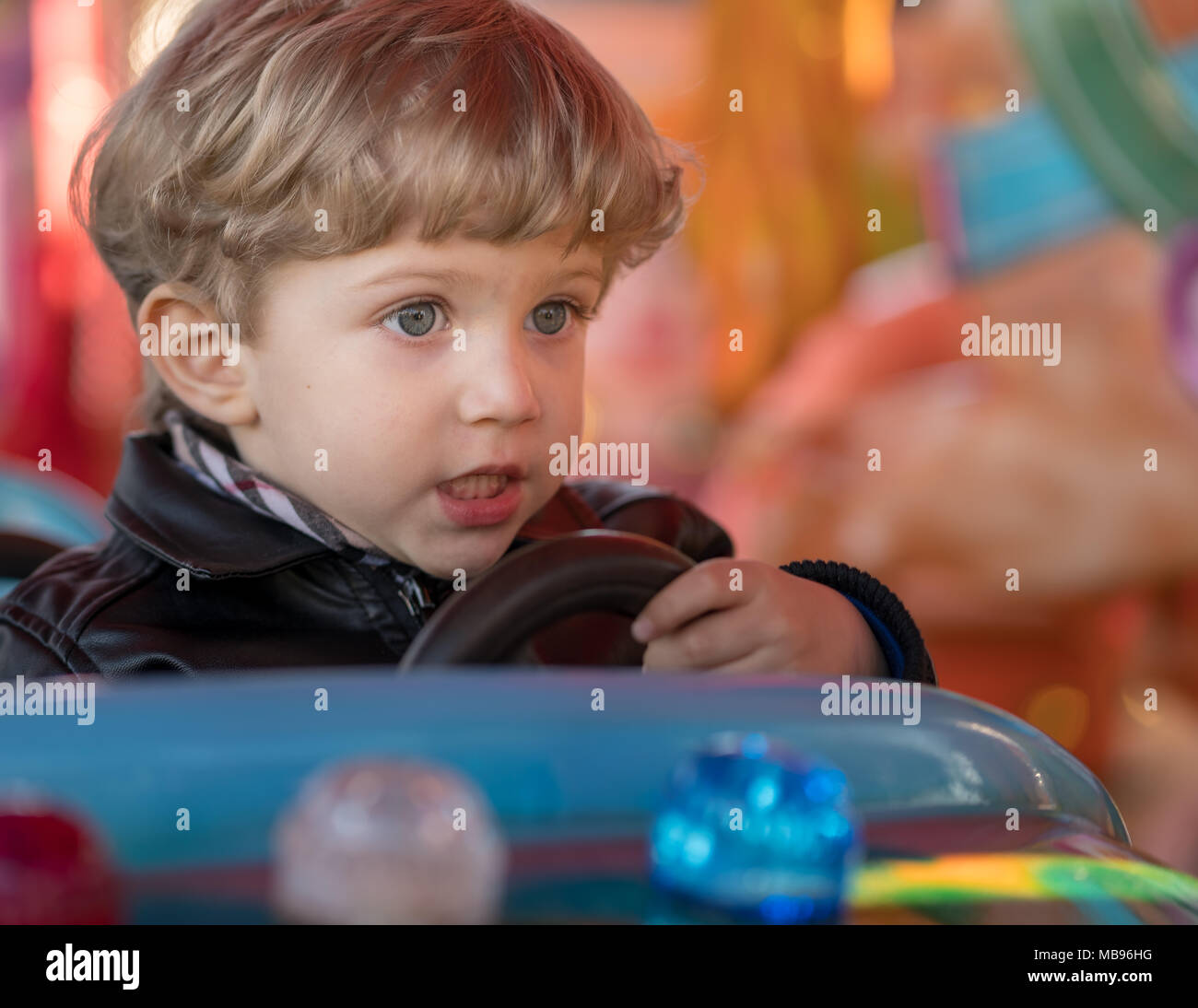 Little boy riding a blue car in the amusement theme park. Happy toddler ...