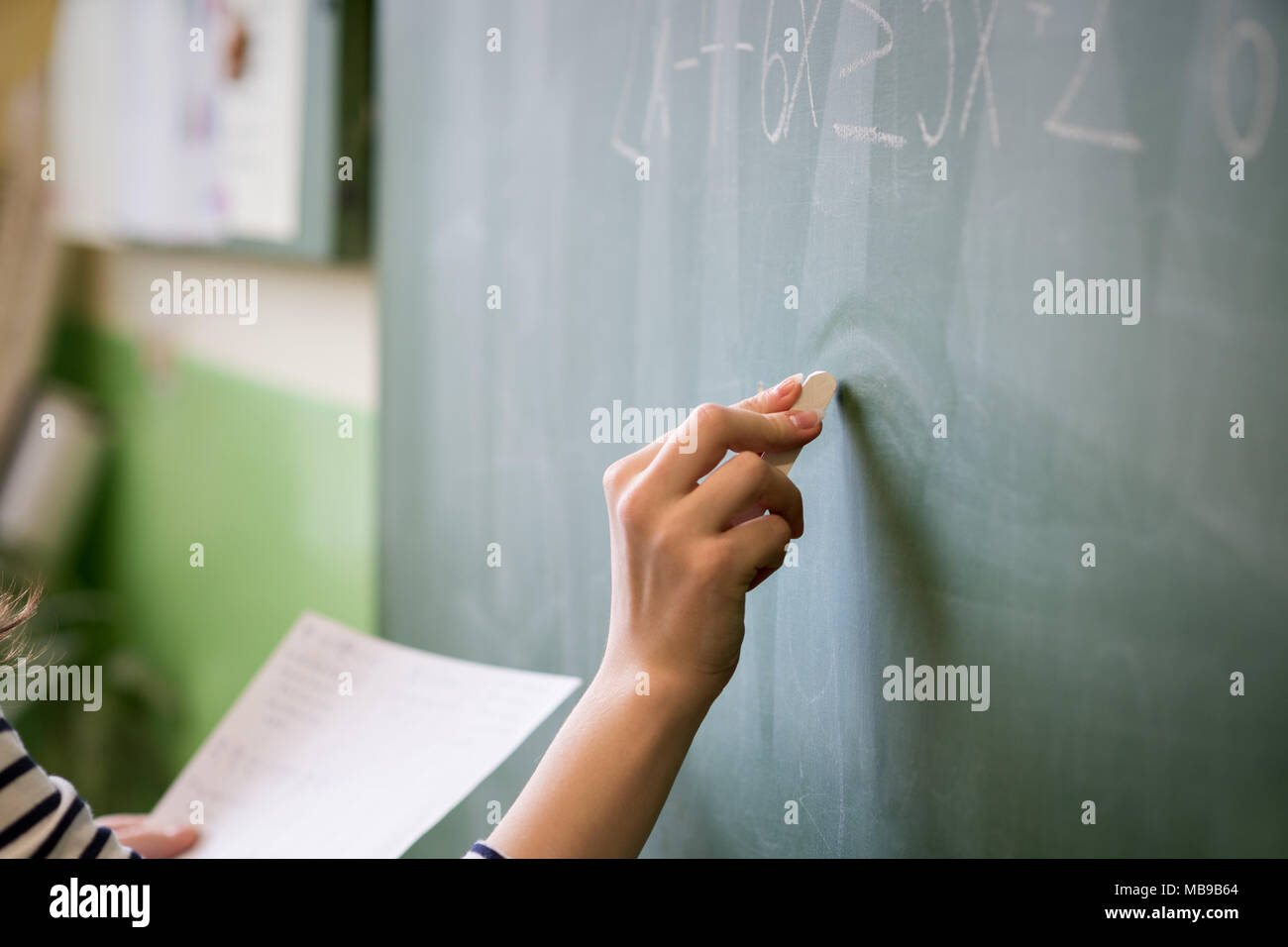 Young female teacher or a student writing math formula on blackboard in ...