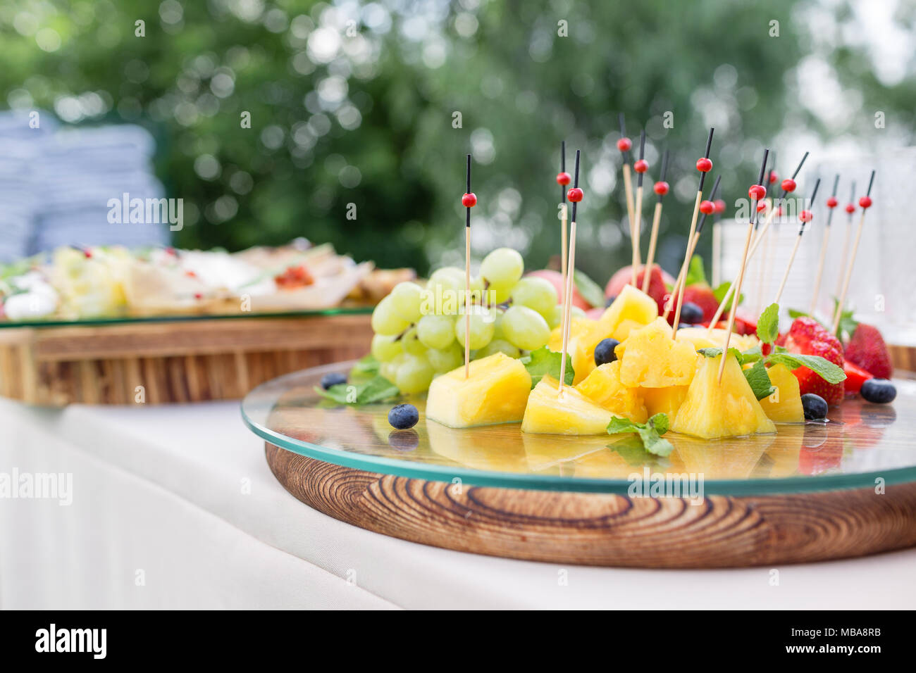 Wooden plate with sliced fruits and berries on a buffet table. Summer ...