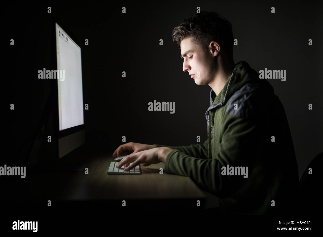 Focused young man using computer in dark room at home Stock Photo - Alamy