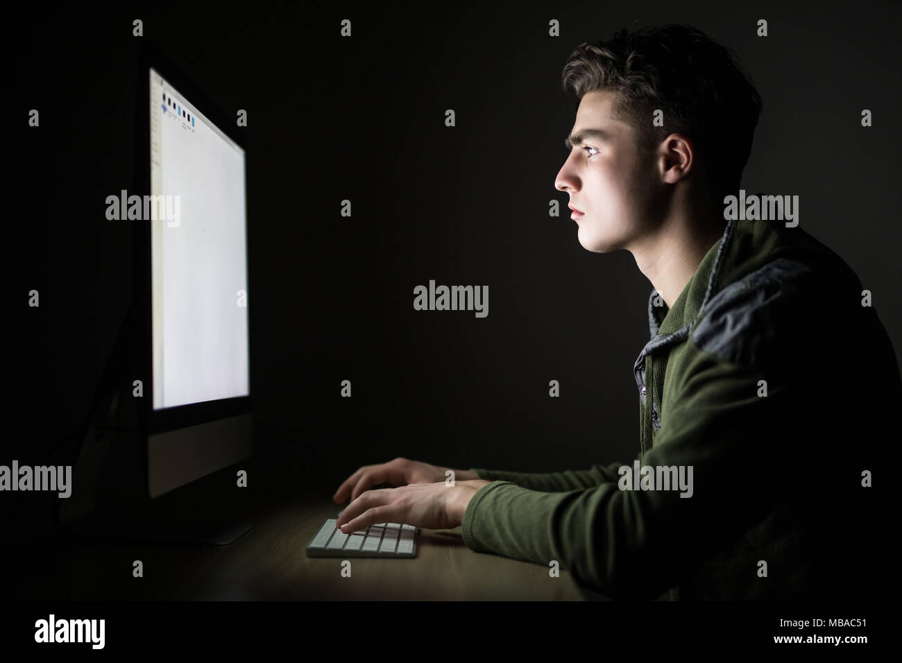 Focused young man using computer in dark room at home Stock Photo - Alamy